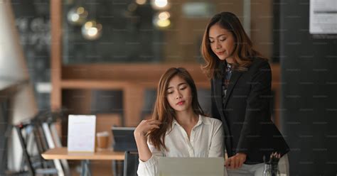 검은 양복을 입은 자신감 있는 비즈니스 여성이 서서 현대적인 사무실 배경 위에 앉거나 포즈를 취하는 아름다운 흰색 셔츠 직원에게 조언합니다 사진 Unsplash의 태국 이미지