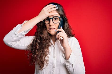 머리에 손으로 스트레스 부끄러움과 깜짝 얼굴 분노와 좌절에 충격 스마트 폰에 대화를 가진 곱슬 머리를 가진 젊은 아름다운 여자 실수에 대한 두려움과 화가 걱정하는에 대한