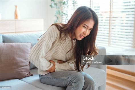 복통을 앓고 있는 젊은 아시아 여성은 집 거실의 소파에 앉아 복통 위염 고통스러운 생리 개념을 앓고 있다 위통에 대한 스톡 사진 및 기타 이미지 Istock