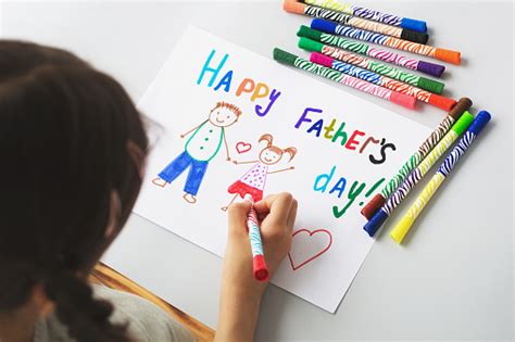 소녀 딸은 아버지의 날을 위해 아빠에게 카드를 그리고 여러 가지 빛깔의 펠트 펜으로 흰 시트에 아빠와 딸을 그리고 달콤한 소원의 개념을 그립니다 개념에 대한 스톡 사진 및