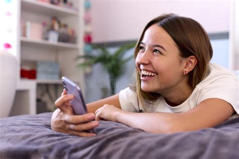Smiling Teenage Girl Lying On Bed At Home Looking At Mobile Phone Stock