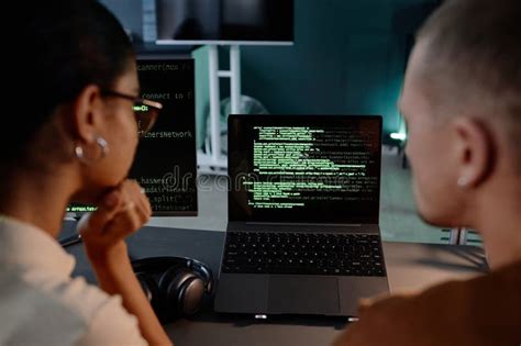 Female It Programmer Looking At Laptop Screen Discussing With Colleague Code In Office Stock