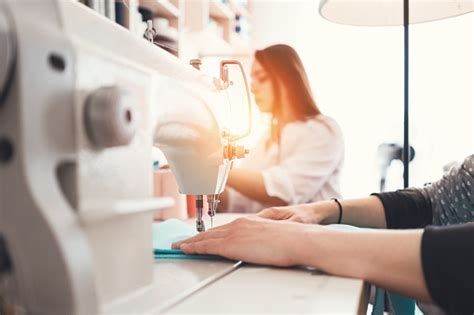 젊은 여자의 근접 촬영 사진 앉아 손 재 봉사 및 창조적인 디자이너 스튜디오에서 재봉틀에 Sews 새로운 의류를 만드는 두 젊은 사업가 양 장점 2명에 대한 스톡 사진 및