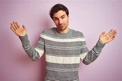 캐주얼 스트라이프 스웨터를 입은 젊은 잘생긴 남자는 고립 된 분홍색 배경 에 서 단서와 팔과 손을 들고 혼란 스러운 표정 의심 개념 감정에 대한 스톡 사진 및 기타 이미지