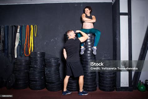 체육관에서 임산부를위한 운동과 운동 백인 선수 Bodybuilders 부부 남편과 아내는 임신을 즐기고 바벨과 아령 장비 근처에서 훈련 후 포즈를 취합니다 2명에 대한 스톡