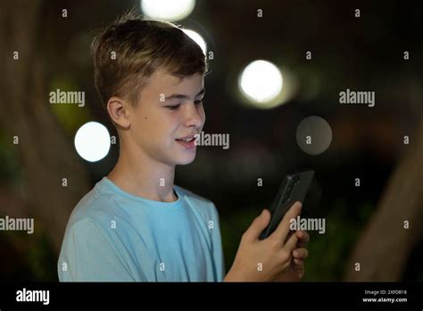 Teenage Boy Texting With His Friend On Cellphone Outdoors On Night City