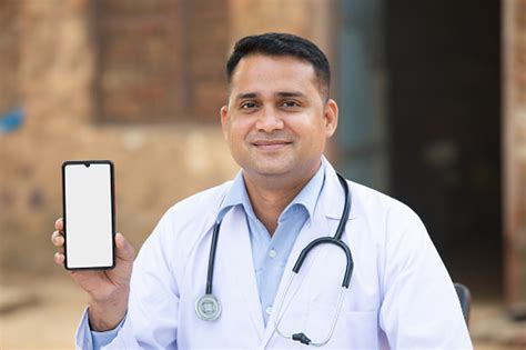 젊은 긍정적인 인도 남성 의사가 청진기를 착용하고 빈 디스플레이 화면이 있는 스마트폰 광고를 위한 휴대폰 모형 시골 의료 개념 30 34세에 대한 스톡 사진 및 기타 이미지