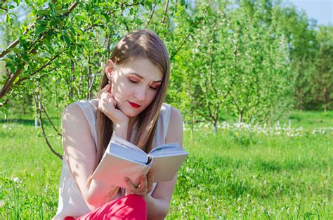 젊은 아주 화창한 날에 꽃이 만발한 사과 나무와 읽기 책 아래 잔디에 앉아 흰 상단과 빨간 바지에 여자 텍스트에 대 한 공간을 복사 개화기에 대한 스톡 사진 및 기타 이미지