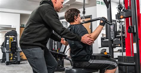 헬스 기구를 사용하는 고객을 돕는 개인 트레이너 · 무료 스톡 사진