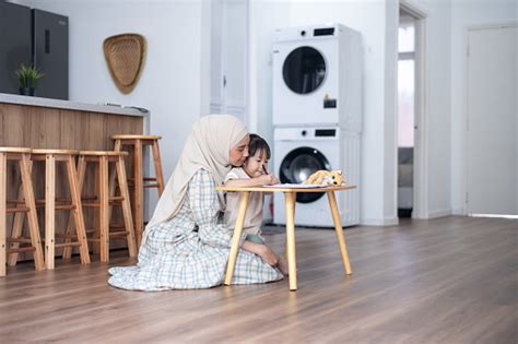 히잡을 쓴 어머니가 어린 딸과 함께 바닥에 앉아 아늑한 집의 나무 탁자에서 함께 학습 활동을 하고 있습니다 2 3 살에 대한