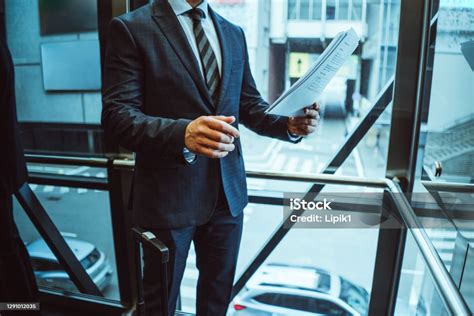 길가가 보이는 현대 사무실에서 가방이 있는 창문 옆에 양복을 입은 사업가를 바라보고 있습니다 창 옆에 있는 서류를 바라보는 사업가 거리에 대한 스톡 사진 및 기타 이미지