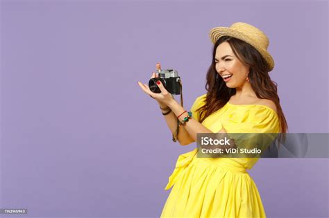 노란 드레스 모자에 쾌활 한 젊은 여자 레트로 빈티지 사진 카메라에 사진을 복용 파스텔 바이올렛 배경에 고립 된 옆에 찾고