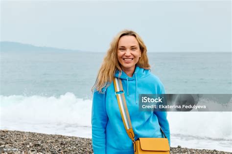 하늘색 후드티를 입은 매력적인 금발 여자가 겨울 해변을 걷고 있다 여행 웰빙과 조화 개념 자연과의 화합 가을에 대한 스톡 사진 및 기타 이미지 Istock