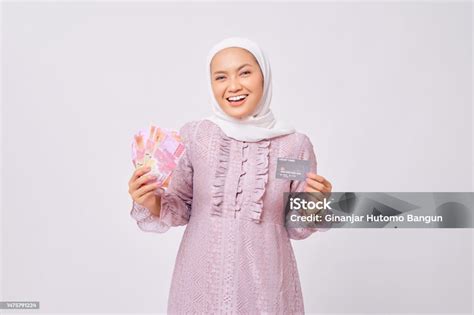 흰색 스튜디오 배경에 격리된 신용 카드와 돈 지폐를 들고 히잡과 보라색 드레스를 입은 쾌활한 젊은 아시아 무슬림 여성 Eid Ul Fitr에 대한 스톡 사진 및 기타 이미지