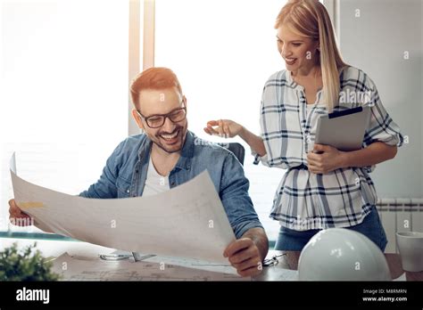 Young Successful Architect Colleagues Talking And Analyzing Blueprints While Working On A New