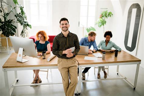 백그라운드에서 동료들과 함께 회의실에서 카메라에 미소 짓고 서있는 자신감있는 젊은 사업가 개성 개념에 대한 스톡 사진 및 기타