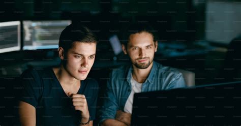 프로그래머는 사무실에서 컴퓨터를 보고 일하고 있습니다 캐주얼한 잘생긴 젊은이들은 저녁에 직장에 앉아 컴퓨터 작업을 하면서