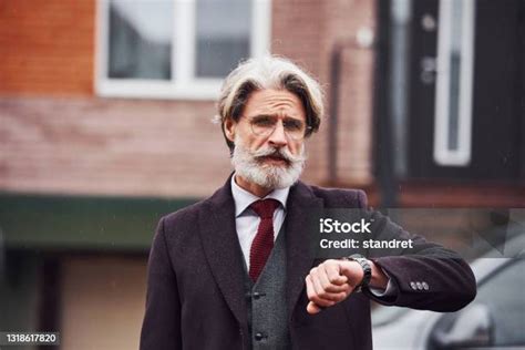 회색 머리와 수염을 가진 세련된 노인은 그의 시계에 시간을 Cheks 근처 거리에 야외 45 49세에 대한 스톡 사진 및 기타 이미지 45 49세 거리 교통수단