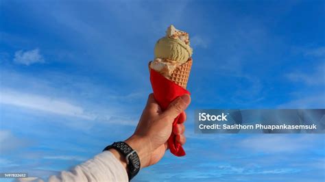 파란 하늘 배경의 마카다미아 견과류와 바닐라 와플 콘으로 맛있는 아이스크림을 들고 있는 남자의 손 거품 내기에 대한 스톡 사진