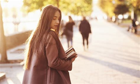 젊은 예쁜 갈색 머리 소녀 턱 아래 그녀의 두 손으로 벽에 기대어 복사 공간 흐린 배경에가을 화창한 공원 캐주얼 코트를 입고