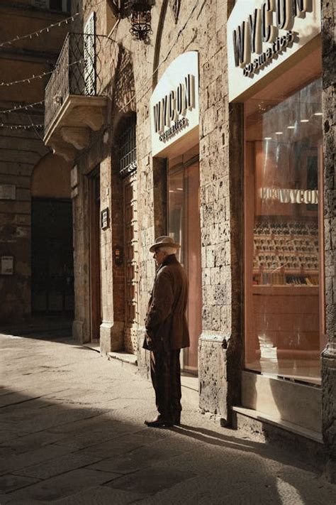 모자를 쓴 우아한 남자가 역사적인 건물 옆에 서 있다 · 무료 스톡 사진