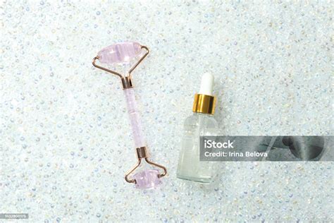 분홍색 마사지 석영 롤러와 흰색 진주가있는 밝은 배경에 액체 젤이있는 투명 유리 화장품 병 노화 방지 얼굴 마사지와 휴식 구아 샤 마사지 도구 메이크업 화장품에 대한 스톡