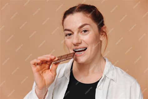 Premium Photo Portrait Of Mature Woman In Braces Biting Chocolate On
