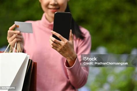 스마트폰과 신용 카드로 온라인으로 결제하는 쇼핑백을 들고 있는 스미진 여성의 잘린 사진 25 29세에 대한 스톡 사진 및 기타 이미지 25 29세 Po
