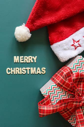 청록색 배경에 컷 아웃 흰색 글자와 수제 Diy 쉬운 크리스마스 카드 디자인의 이미지 수제 축제 크리스마스 인사말 카드 산타 모자와 포장 선물과 활 복사 공간 메리