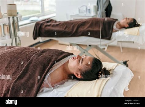 Young Woman Wrapped In Foil And Towel Relaxing On Massage Table During