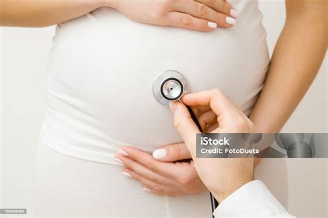 닥터 남자의 손 검사 하 고 젊은 여자 큰 배꼽에 청진 기 아기 심장 박동을 듣고 정기적인 검사 임신 시간20 주 아기 기대