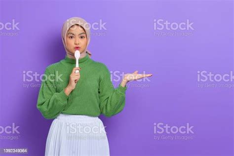 녹색 스웨터와 히잡 을 입고 숟가락을 들고 보라색 배경 위에 고립 된 손에 복사 공간을 보여주는 쾌활한 아름다운 아시아 여성 20 24세에 대한 스톡 사진 및 기타 이미지