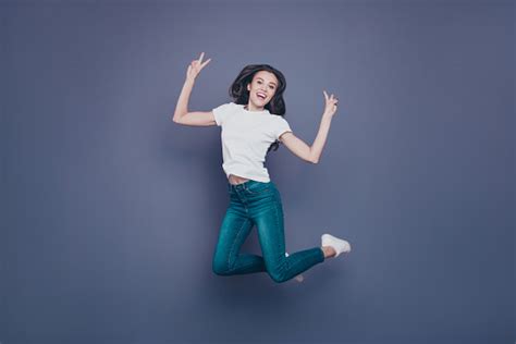 사랑 스럽다 꽤 사랑 스러운 세련 된 좋은 밝은 꿈꾸는 곱슬 머리 갈색 머리 소녀 캐주얼 티셔츠와 청바지 공기 비행에 회색 배경에 고립 된 더블 Vsign T 셔츠에 대한