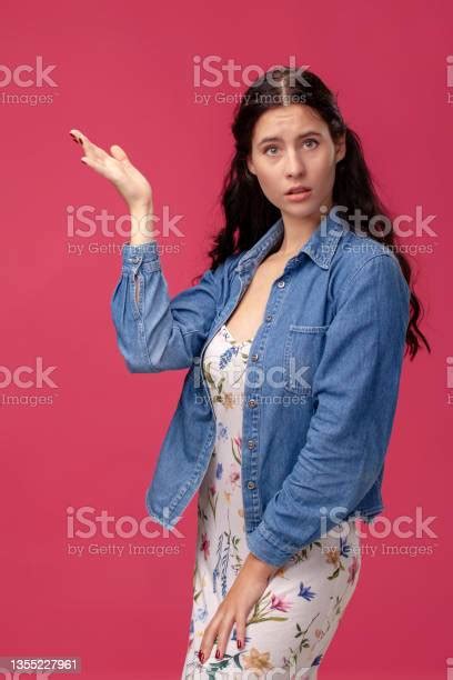 스튜디오에서 분홍색 배경에 서 밝은 드레스와 파란색 셔츠를 입은 예쁜 젊은 여성의 초상화 진지한 감정 갈색 머리에 대한 스톡 사진 및 기타 이미지 Istock
