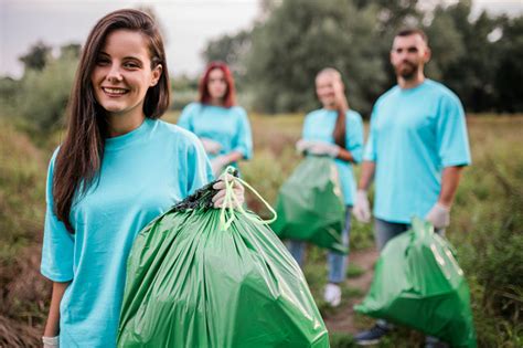 장갑과 쓰레기 봉투를 든 작은 그룹의 자원 봉사자가 방금 청소한 공원에서 멈추는 자연스러운 이미지 청바지와 파란색 티셔츠를 입은 모든 사람들은 지금까지 한 일에 대해