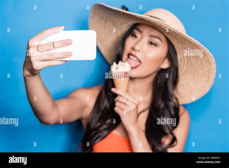 Beautiful Asian Woman In Swimsuit And Beach Hat Licking An Ice Cream And Taking Selfie With Her