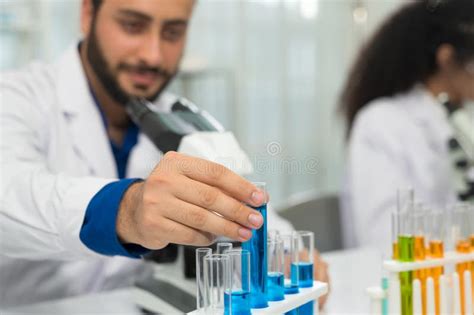 Male Scientist In White Lab Coat Examines Bright Blue Liquid In Test