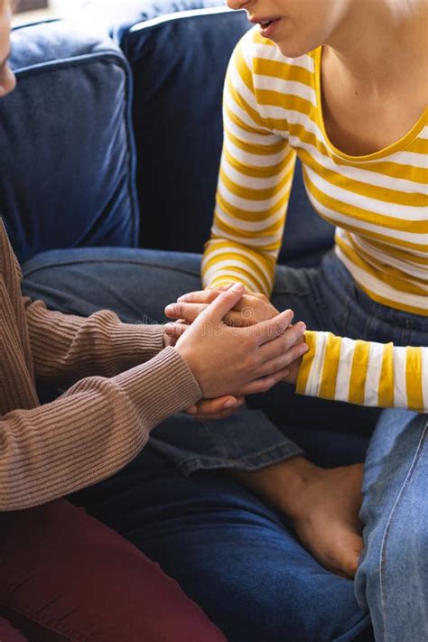 Midsection Of Biracial Lesbian Couple Holding Hands Sitting On Couch