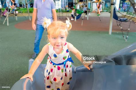 귀여운 작은 미소 Blondy 유아 소녀 드레스는 배경에서 그녀의 아버지와 함께 Momern 여름 놀이터에 어린이 언덕에