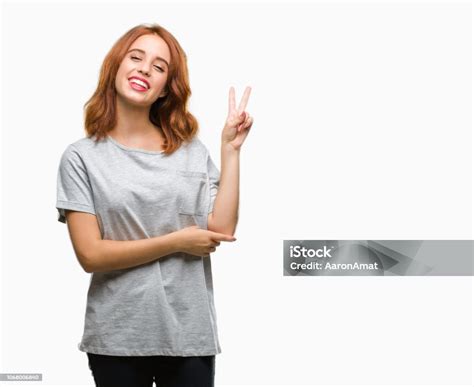 승리 표시를 하 고 카메라에 윙크 하는 행복 한 얼굴로 웃 고 고립 된 배경 위에 젊은 아름 다운 여자 번호 2입니다 긍정적인 감정 표현에 대한 스톡 사진 및 기타 이미지
