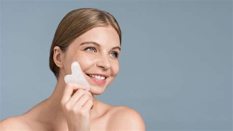 Gua Sha를 사용하여 얼굴 마사지를 하는 파란 눈을 가진 젊은 백인 여성 무료 사진