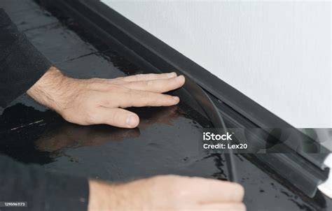 한 남자가 흰색 벽지벽과 나무로 칠해진 바닥을 따라 검은 색 Pvc 스커트 보드를 설치하여 플라스틱 성형 뒤에 전기 케이블을