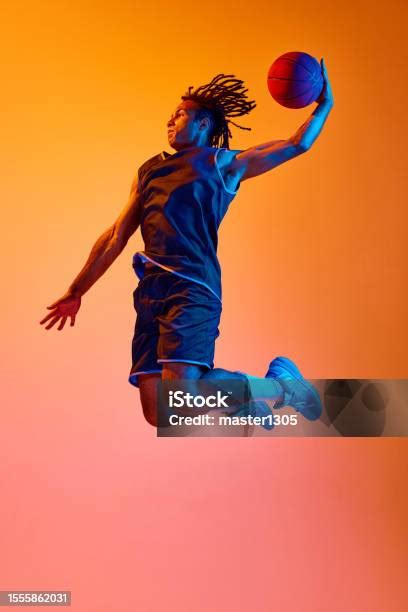 젊은 스포츠맨 움직이는 농구 선수 네온 불빛의 주황색 배경에 공을 들고 점프하는 전체 길이 이미지 스포츠에 대한 스톡 사진 및 기타 이미지 Istock