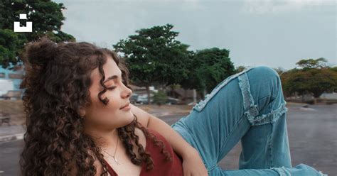 빨간 탱크탑과 파란색 데님 청바지를 입은 여자가 낮 동안 회색 콘크리트 바닥에 앉아 있다 사진 Unsplash의 무료 브라질 이미지