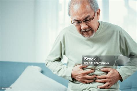 아시아 노인은 복통을 느낍니다 나이가 많은 성숙한 남성은 집에서 거실의 소파에 앉아있는 동안 배를 만집니다 장 문제 건강 관리 및 의료 보험 개념 변비에 대한 스톡 사진 및