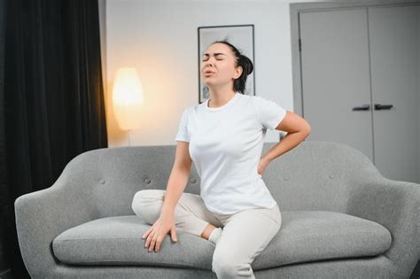 Linda Chica Sentada En La Cama Con Los Ojos Cerrados Mientras Sufre De Dolor De Espalda Foto