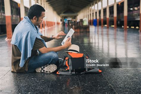 기차역 바닥에 앉아 디지털 태블릿을 가진 젊은 남자 여행자가 어디로 갈지 선택합니다 배낭 여행자의 개념은 기차로 모험을 여행합니다 40 44세에 대한 스톡 사진 및 기타