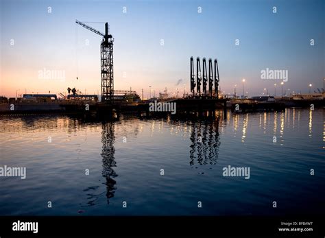 A Tanker Loading And Unloading Dock With Hoist Cranes And Oil Pumps In An Industrial Harbor