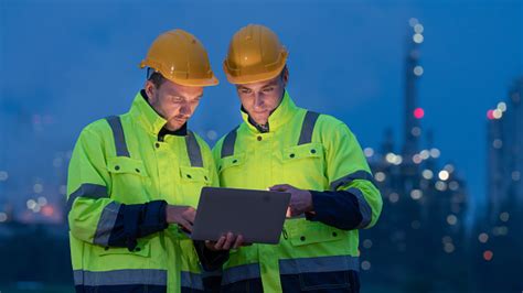 안전복과 헬멧을 착용한 백인 엔지니어들이 현장 통신을 위해 노트북과 라디오를 사용하고 있습니다 산업 시설에서의 팀워크 검사 및 운영의 개념 석유 가스 및 연료 수송 파이프