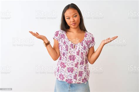 고립된 흰색 배경 위에 서있는 캐주얼 한 꽃 무늬 티셔츠를 입은 젊은 중국 여성은 팔과 손을 들고 혼란스러운 표정을 짓고